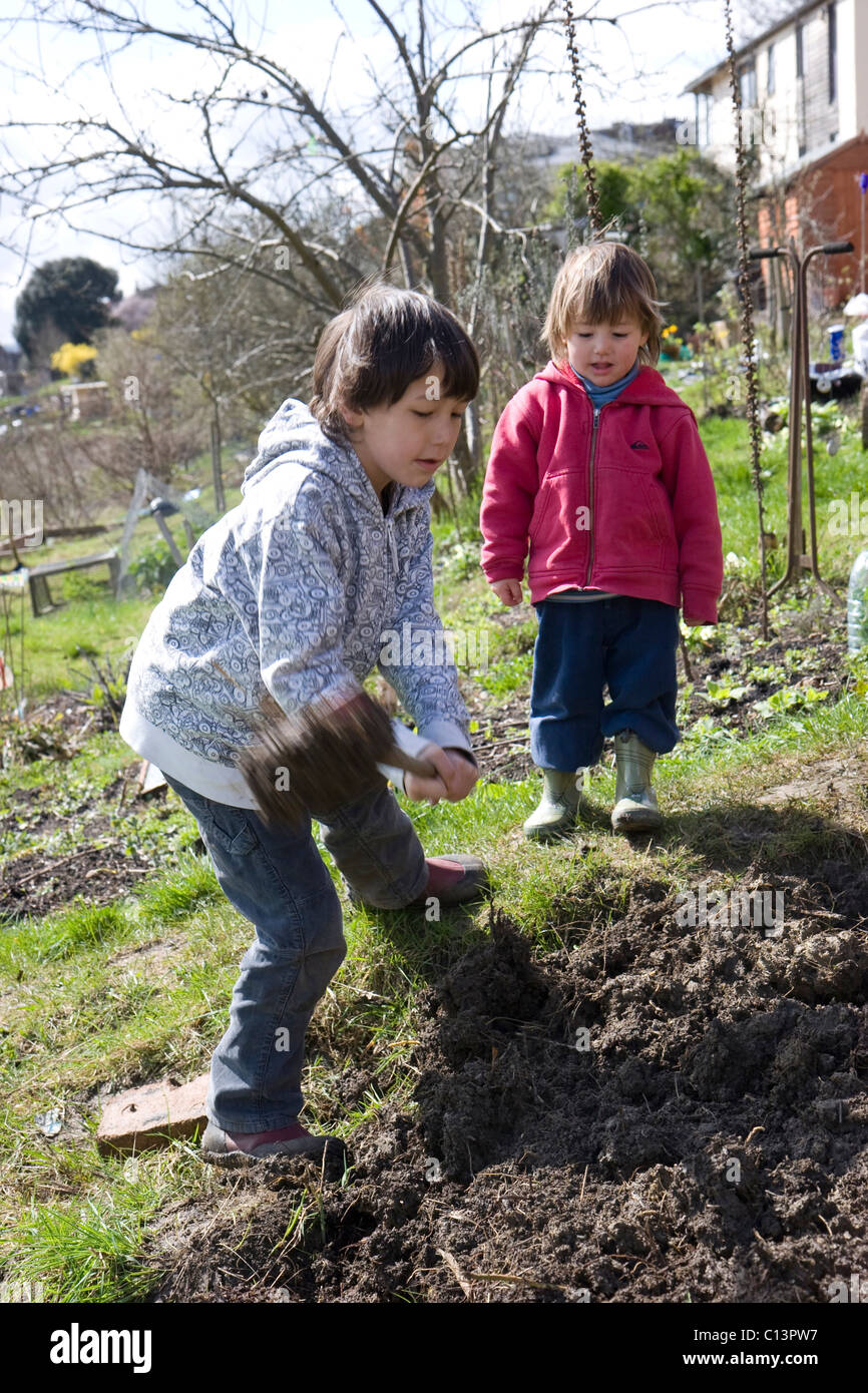 Boy working the soil at city allotment with younger brother watching ...