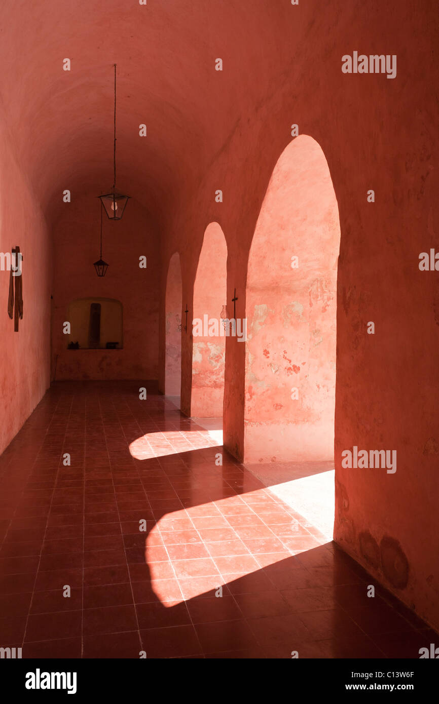 Hallway of the Convent Cloister in red adobe. The sun shines in through ...