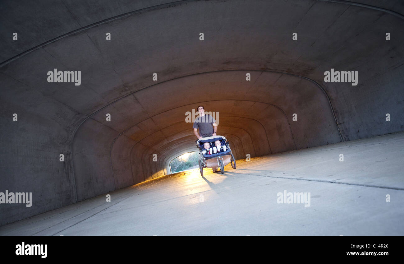 A man exiting a tunnel, running with his twin boys in a stroller in ...