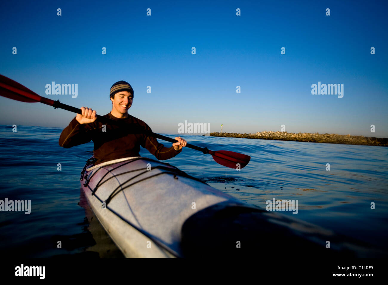A young man smiles while paddling a touring kayak just outside of ...