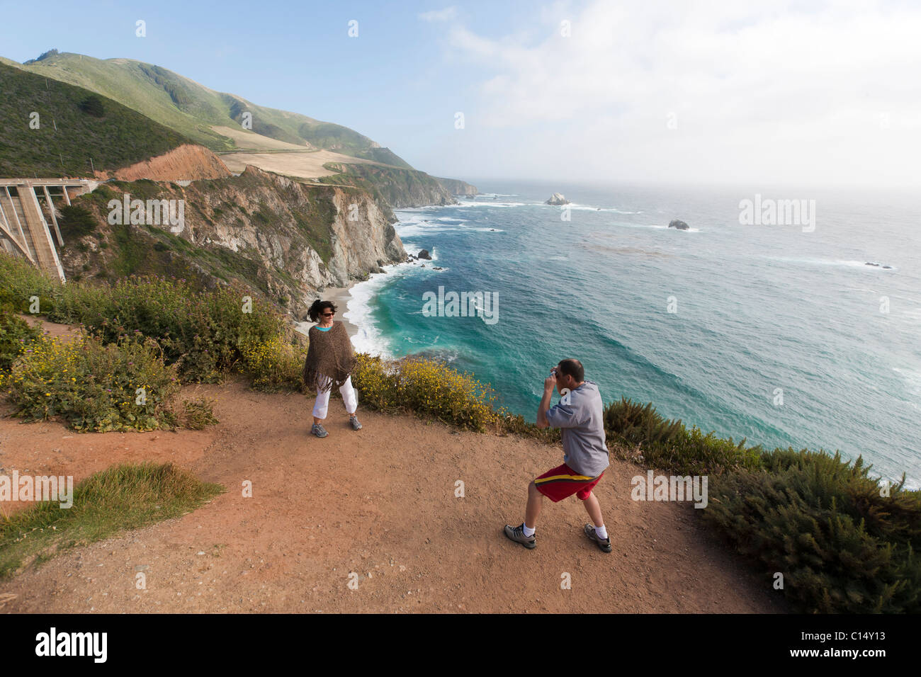 Couple taking photographs on path overlooking rocky cliffs/shoreline of ...