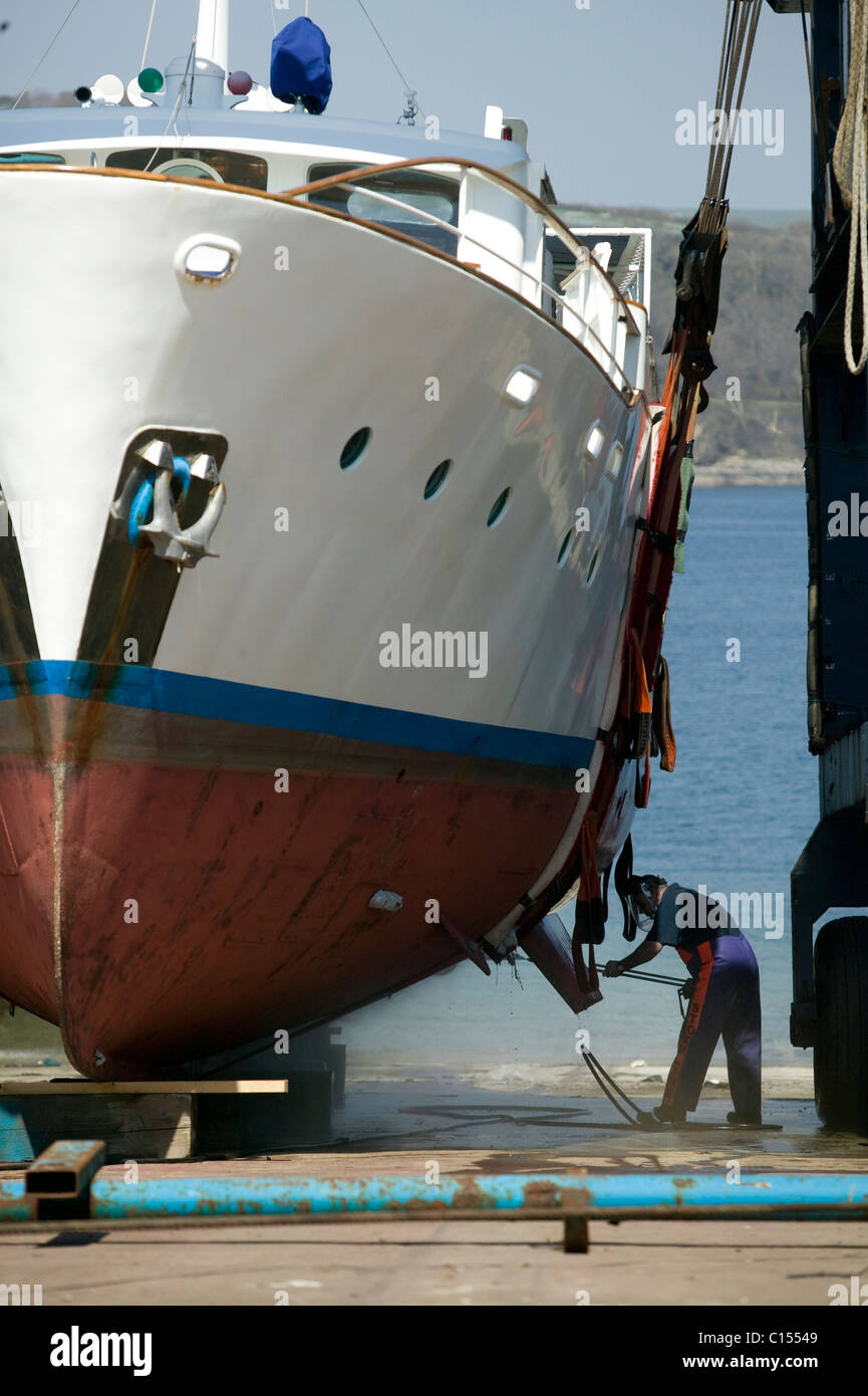 A man working on the hull of a yacht on the slipway at Pendennis ...