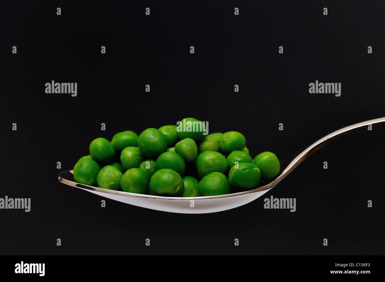 Peas on a spoon against a black background Stock Photo - Alamy