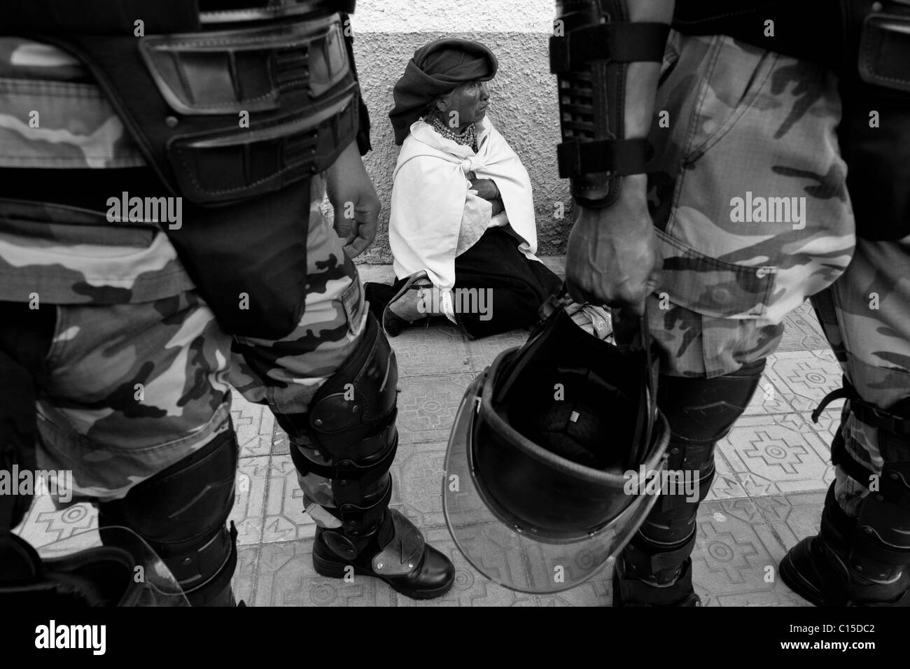 An old Indian woman sits on the pavement behind the riot policemen ...