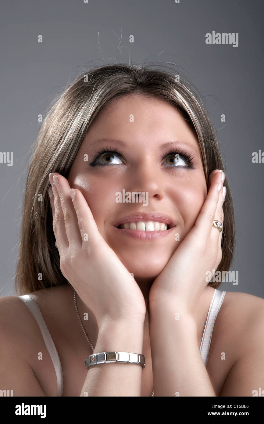 Young woman supporting her head on her hands, looking upwards ...