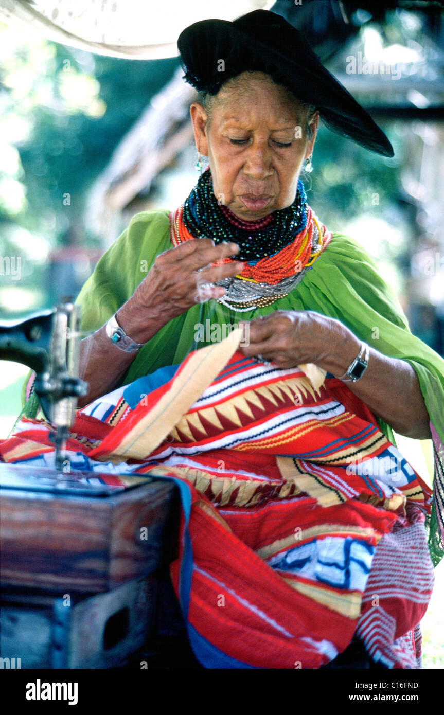 An elderly Miccosukee Indian woman sews traditional clothing outdoors ...