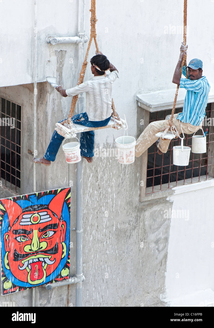 Two indian painters sitting on a wooden seat hanging from ropes ...
