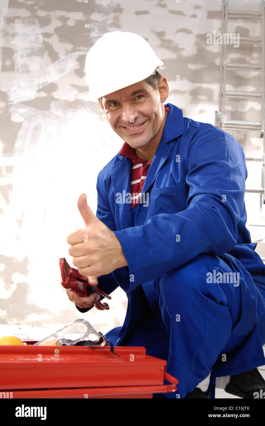 Smiling workman wearing a hard hat kneeling in front of a toolbox ...