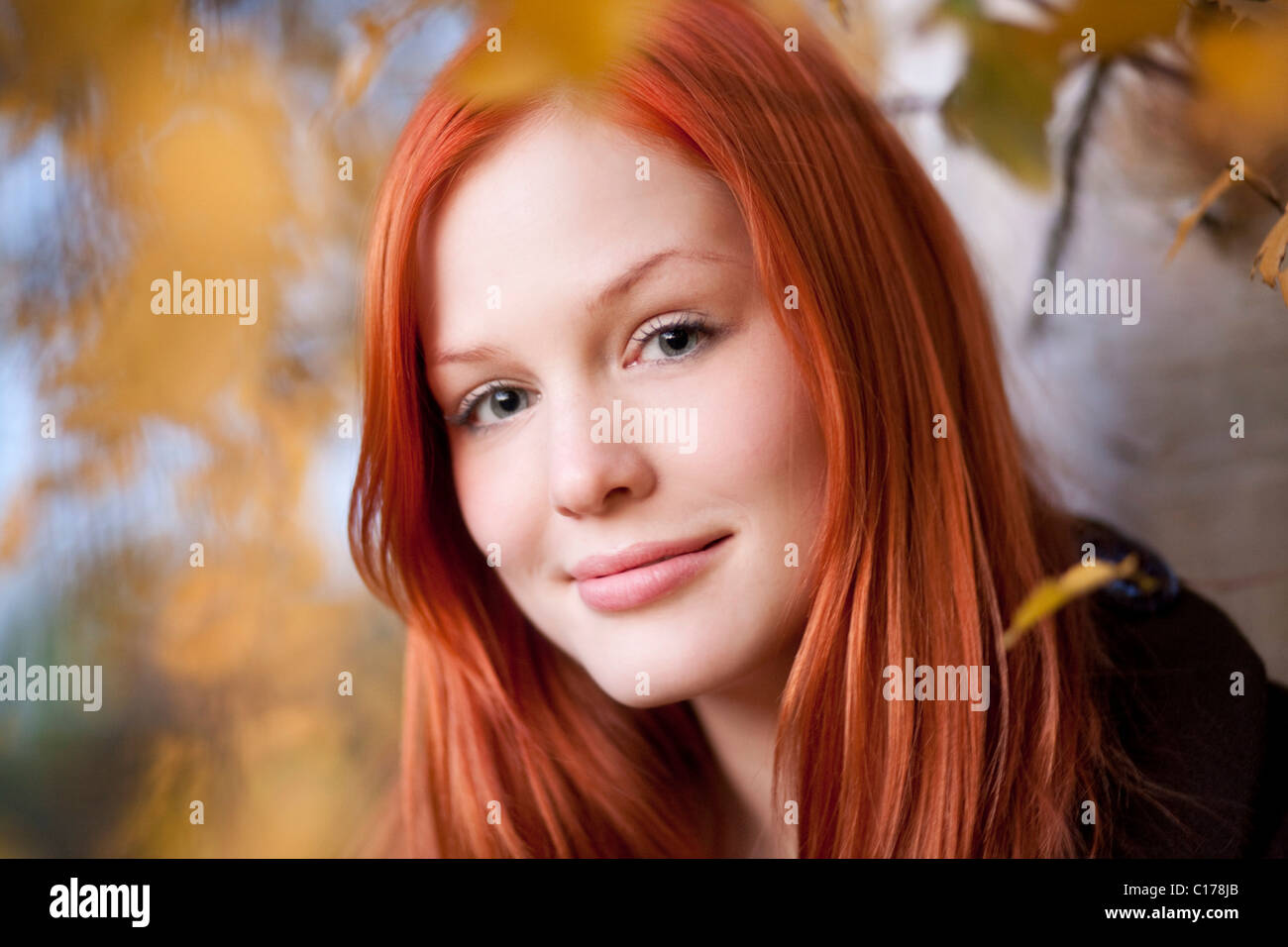 Portrait of a young red haired woman between autumnal leaves in a ...