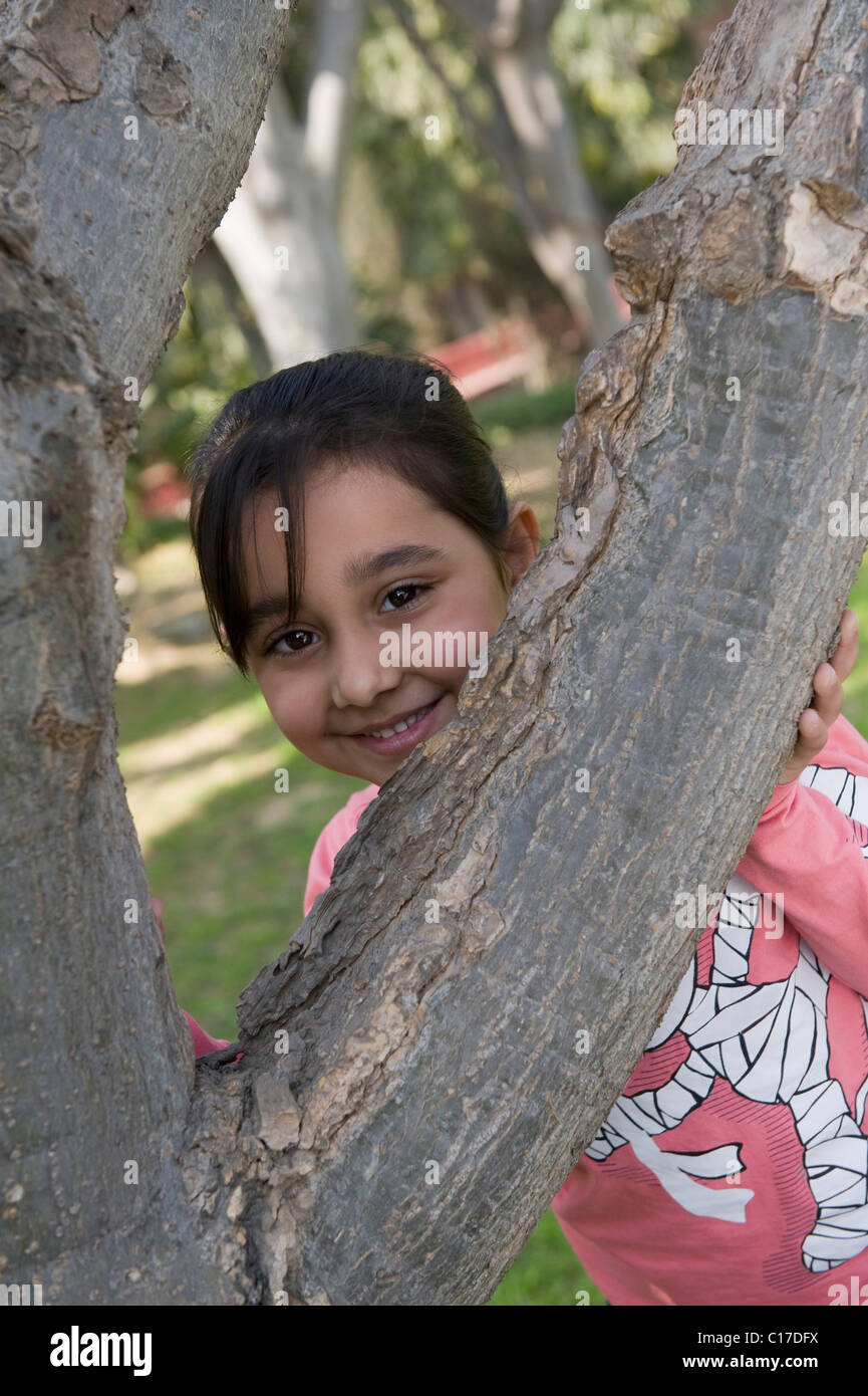 Portrait of a girl smiling behind a tree Stock Photo - Alamy
