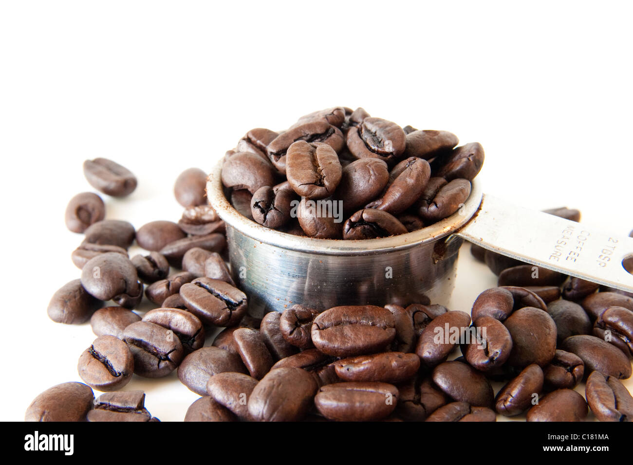 Whole coffee beans spilling out of a full coffee measure. Shot on white ...