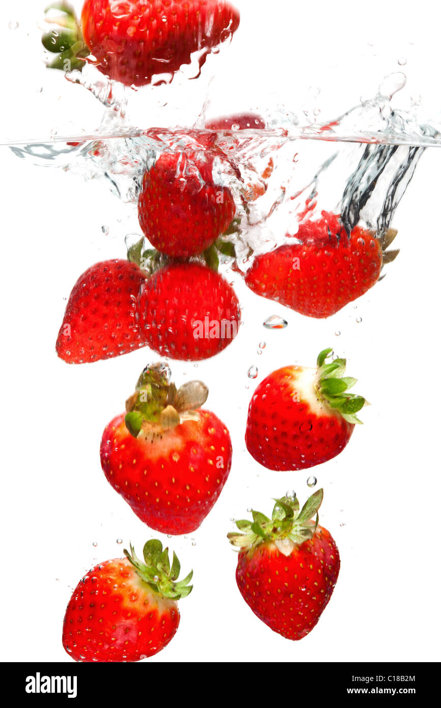Photo of strawberries falling into water against a white background ...