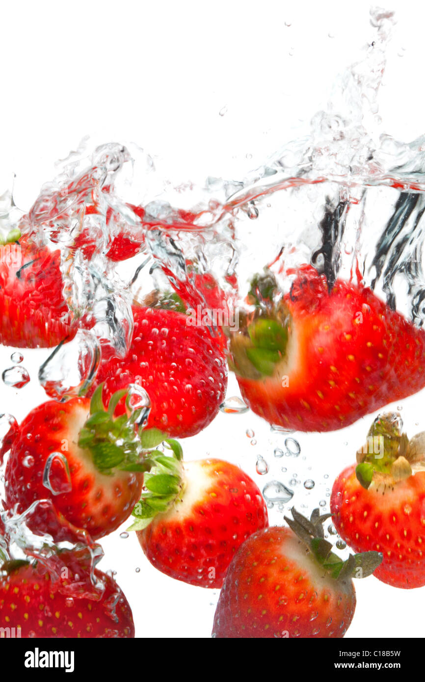 Photo of strawberries falling into water against a white background ...