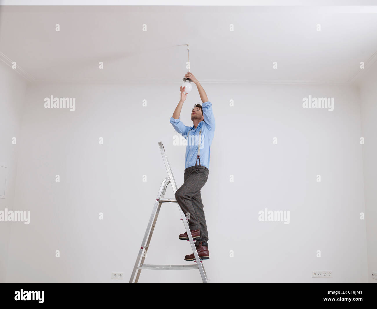 Young man on ladder screws in light bulb Stock Photo - Alamy