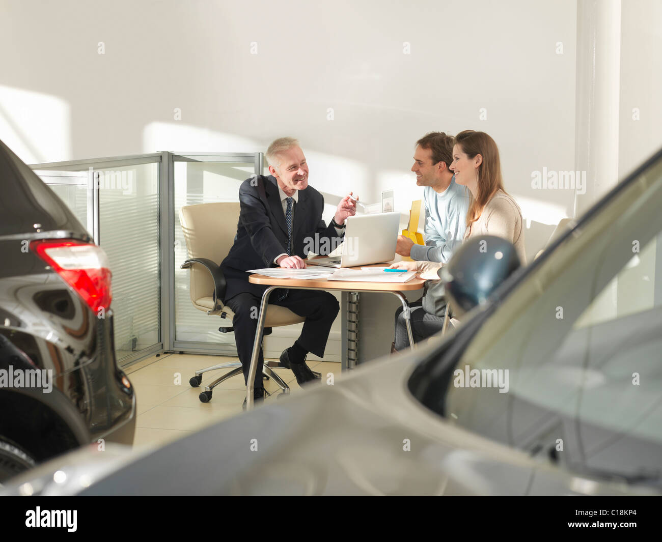 Salesman and customers in car dealership Stock Photo - Alamy
