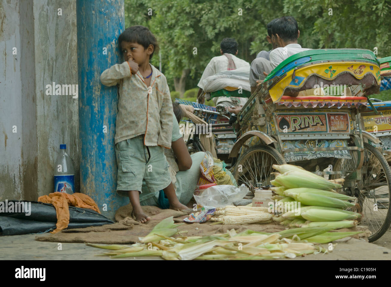 A small, poor boy waits as his mother tries to sell corn in India Stock ...