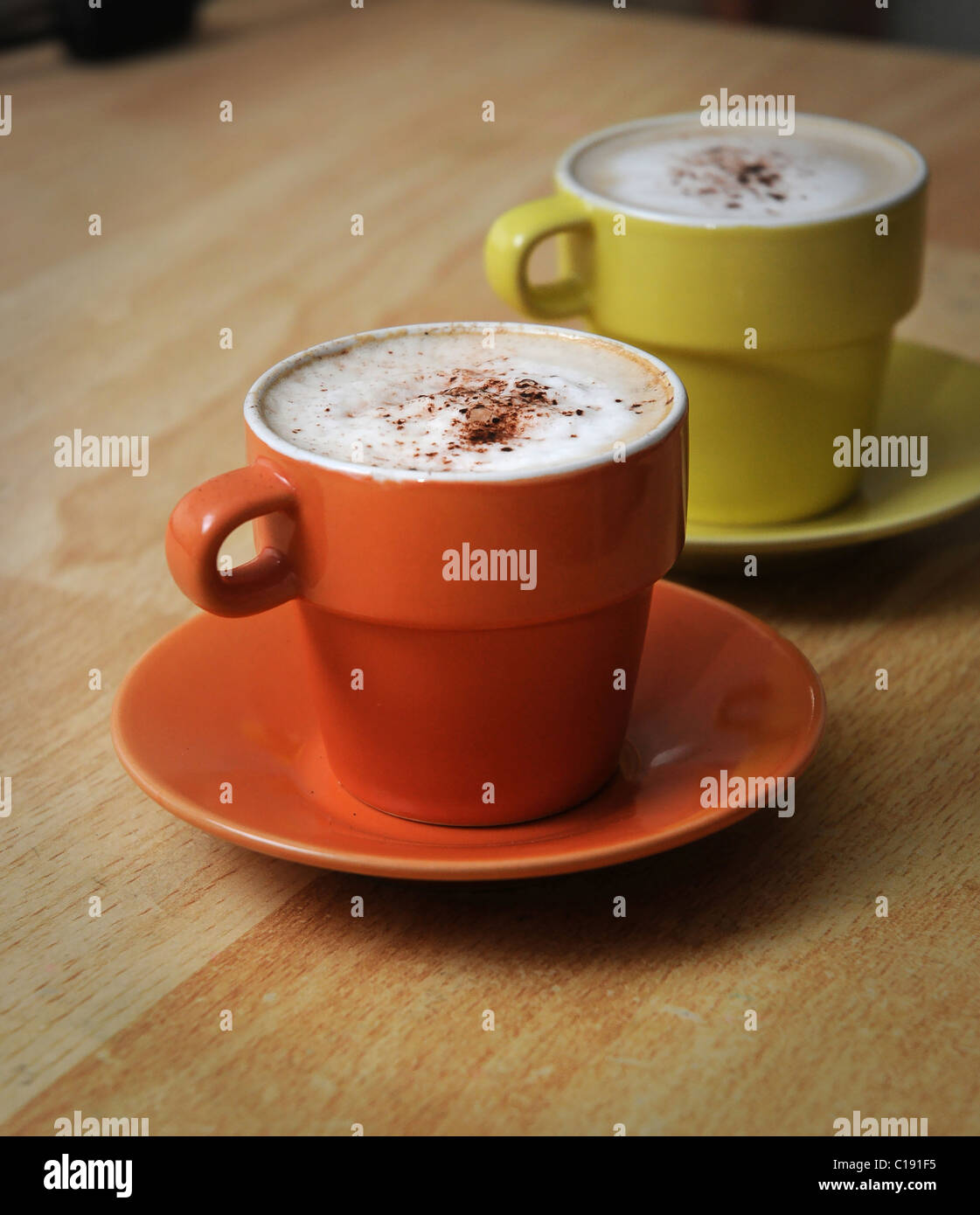 Two cups of cappuccino coffees in an orange and yellow mini mug and ...