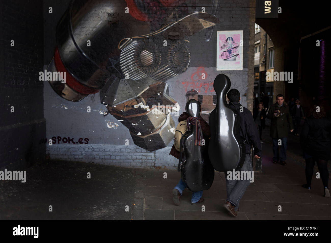 Two cellists carry their large instruments through a dark section of ...