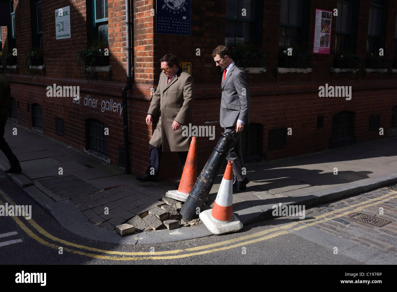 Two male pedestrians walk past a broken post that leans over after ...