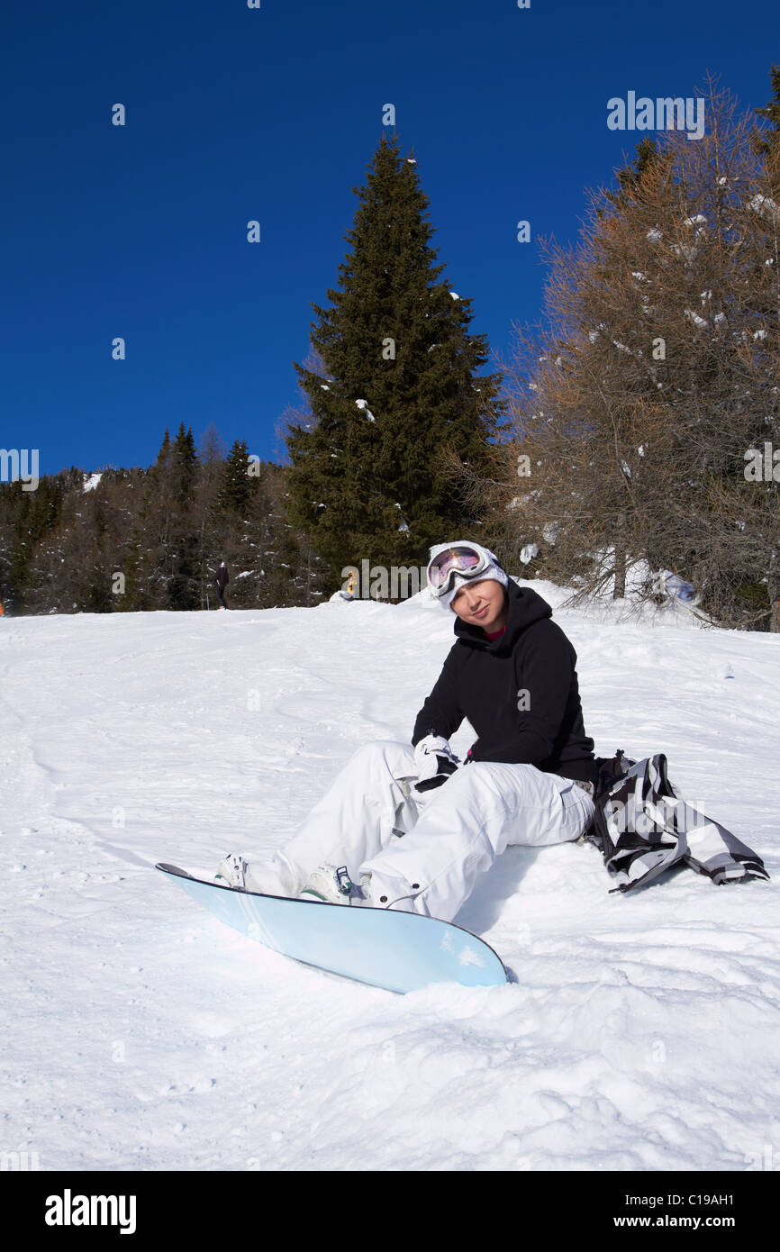 Relaxed female snowboarder sitting among trees Stock Photo - Alamy
