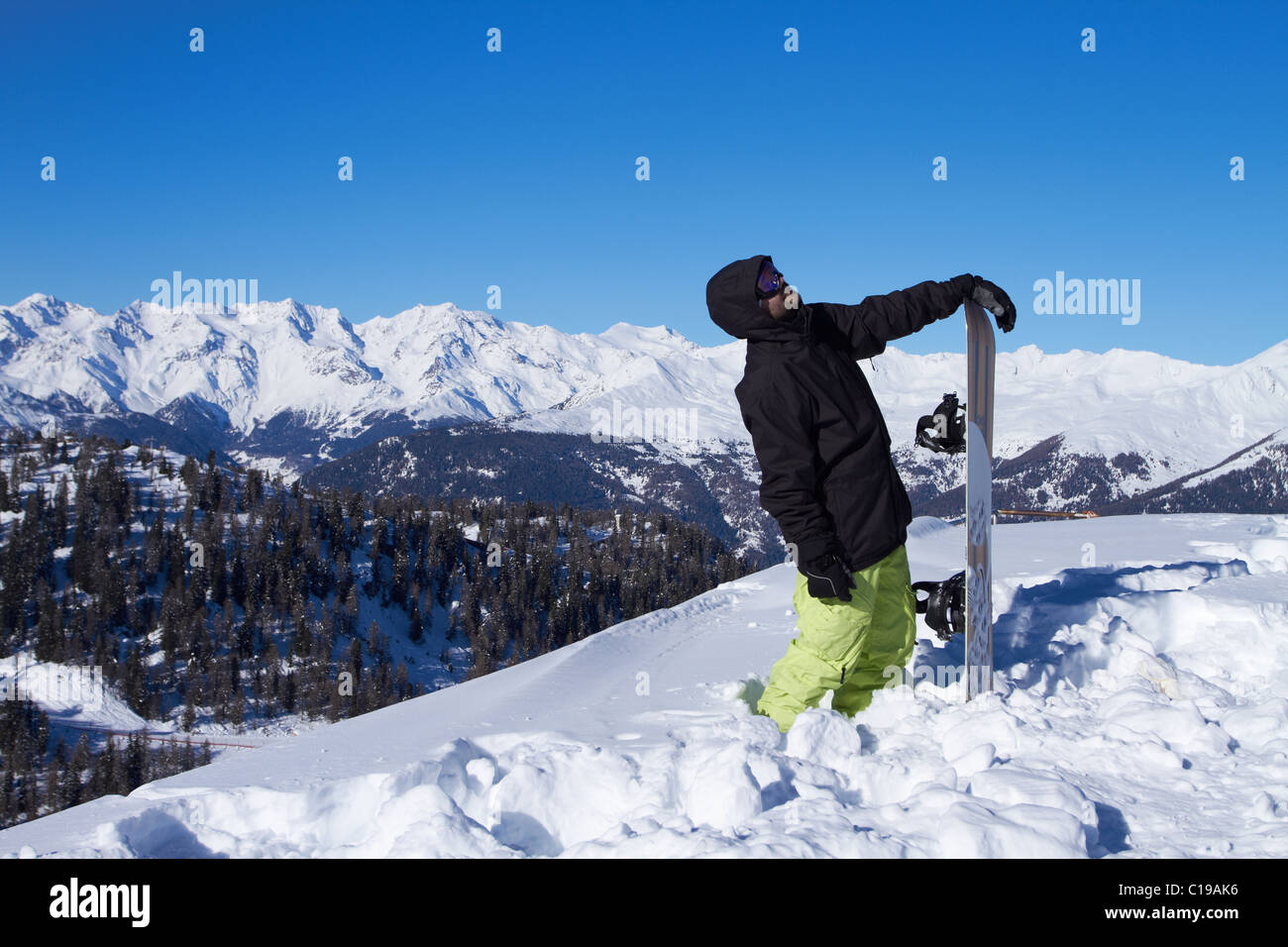 Male snowboarder in the mountains, standing on the top of mountain and ...