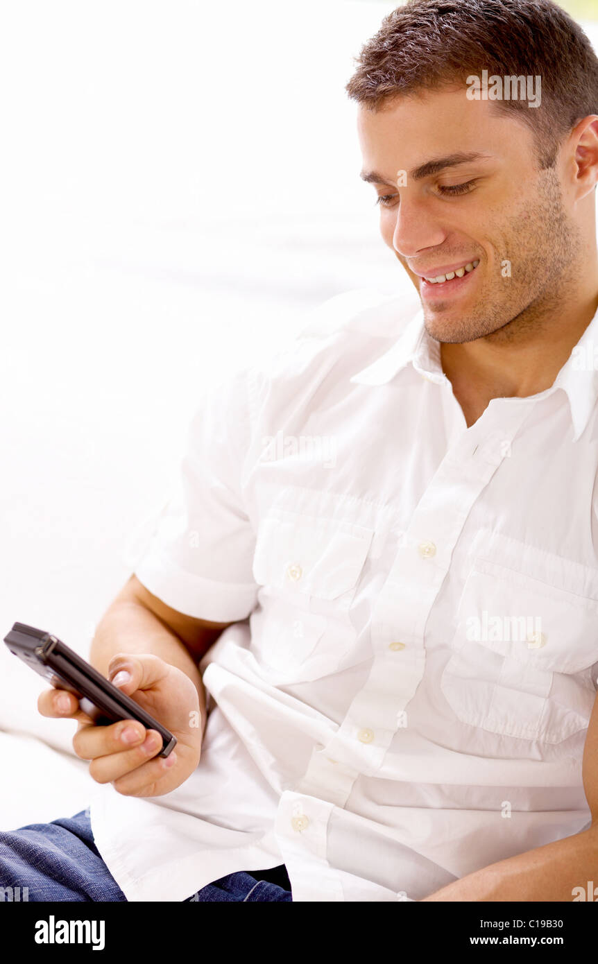 Young man sitting on couch and using cell phone Stock Photo - Alamy
