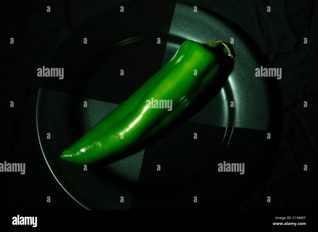 A single pepper on a shiny, black plate Stock Photo - Alamy