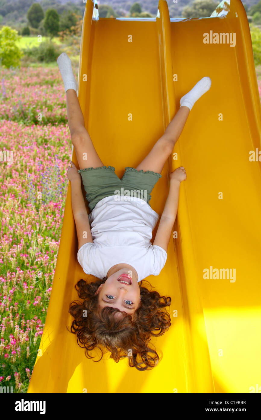Brunette little girl upside down playground slide in pink flower meadow ...