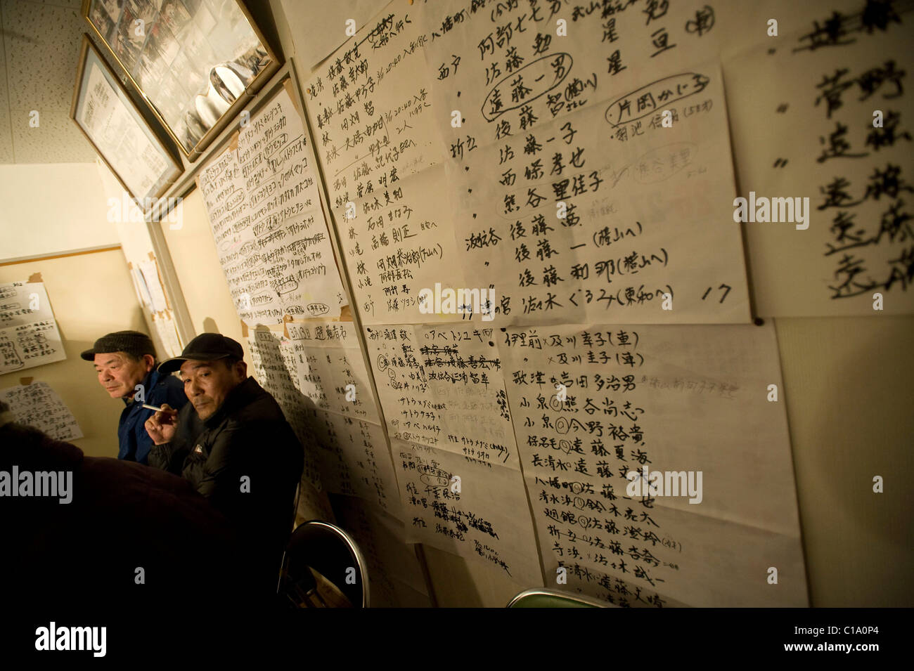 People taking refuge at a shelter sit in front of a list of names of ...