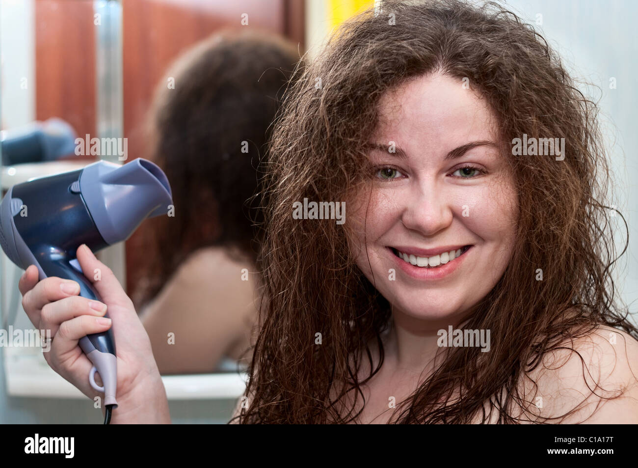 Young Caucasian woman with curly brown bushy hair holding hairdryer ...