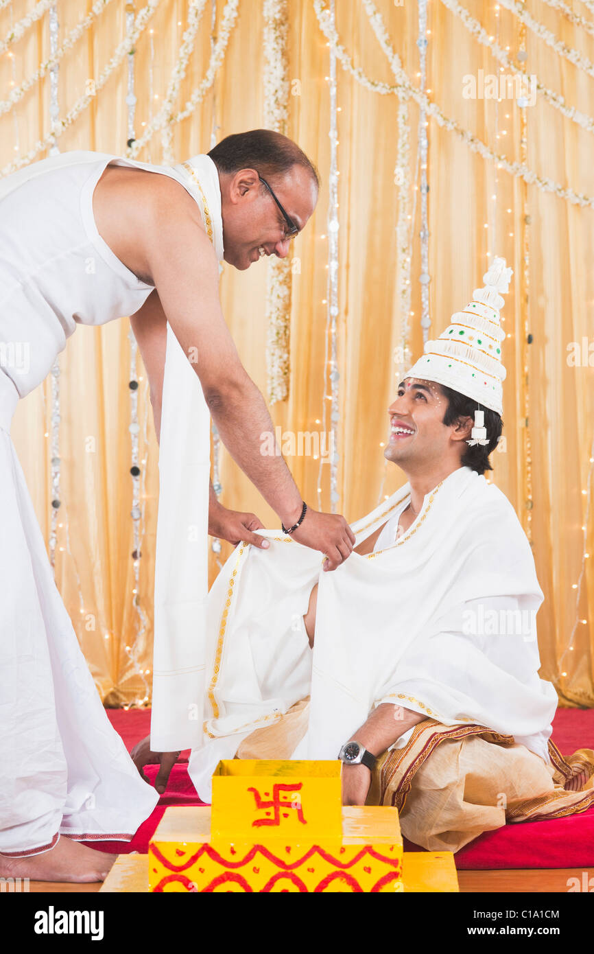 Bridegroom smiling with priest in wedding mandap during Bengali wedding ...
