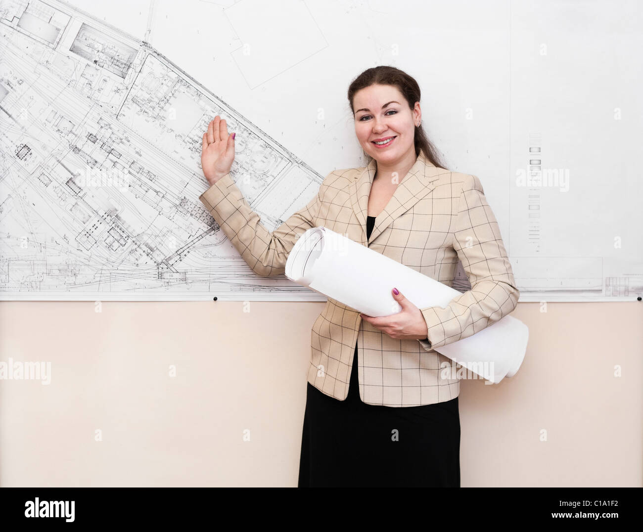 One young woman a architect standing near the big blueprint on wall and ...