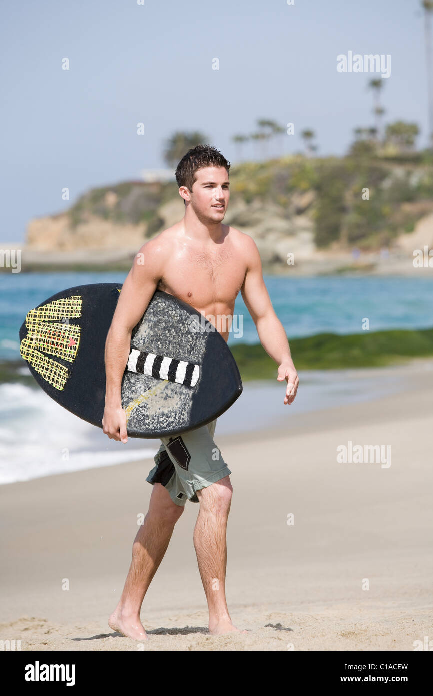 Young man carrying surfboard on beach Stock Photo - Alamy