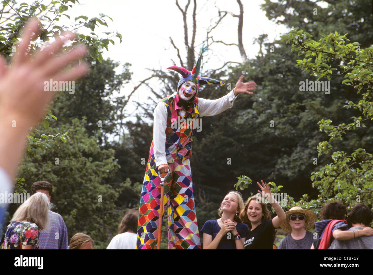 Performing jester clown on stilts waving at crowd and being waved back ...