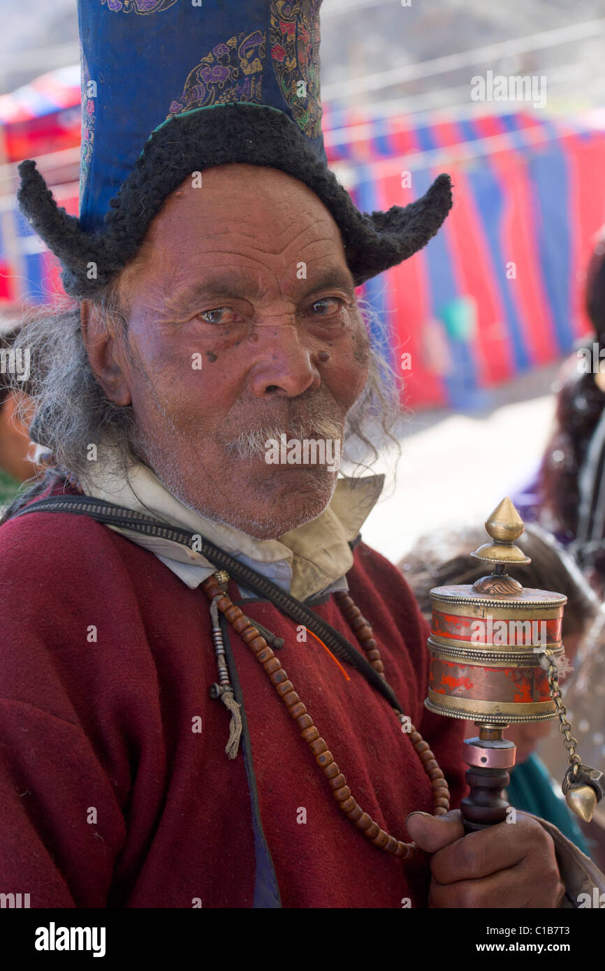 Old Ladakhi man in traditional dress with prayer wheel at a festival to ...