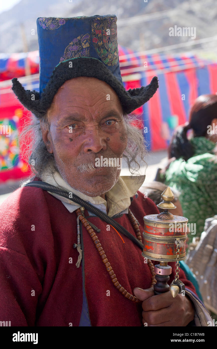 Old Ladakhi man in traditional dress with prayer wheel at a festival ...