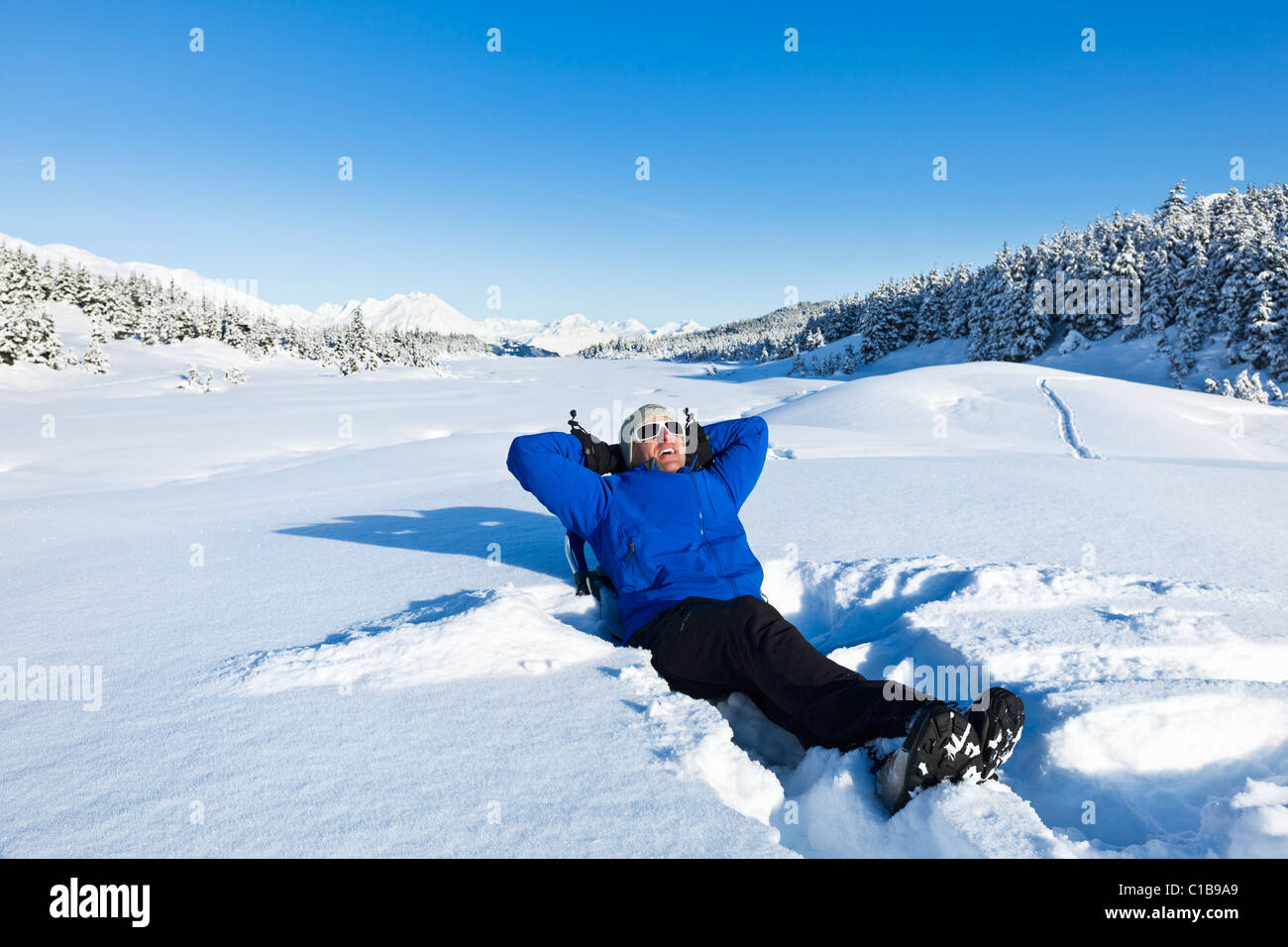 A male hiker reclines against snowshoes on a sunny day in Alaska with ...