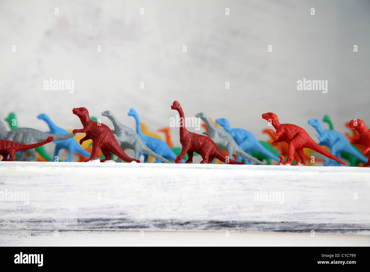 multi coloured miniature plastic dinosaurs marching from right to left ...