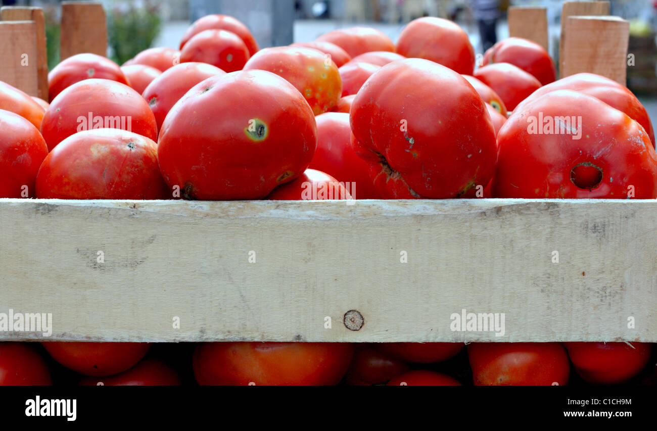 Wooden box full of ripe red non uniform tomatoes on sale at an outdoor ...