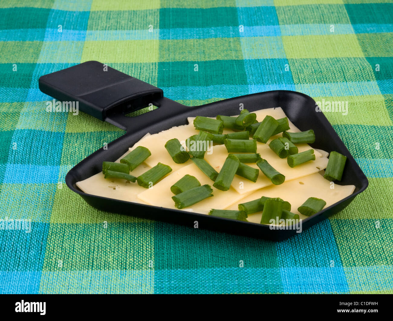 Raclette pan with edam cheese and spring onion on colorful tablecloth ...