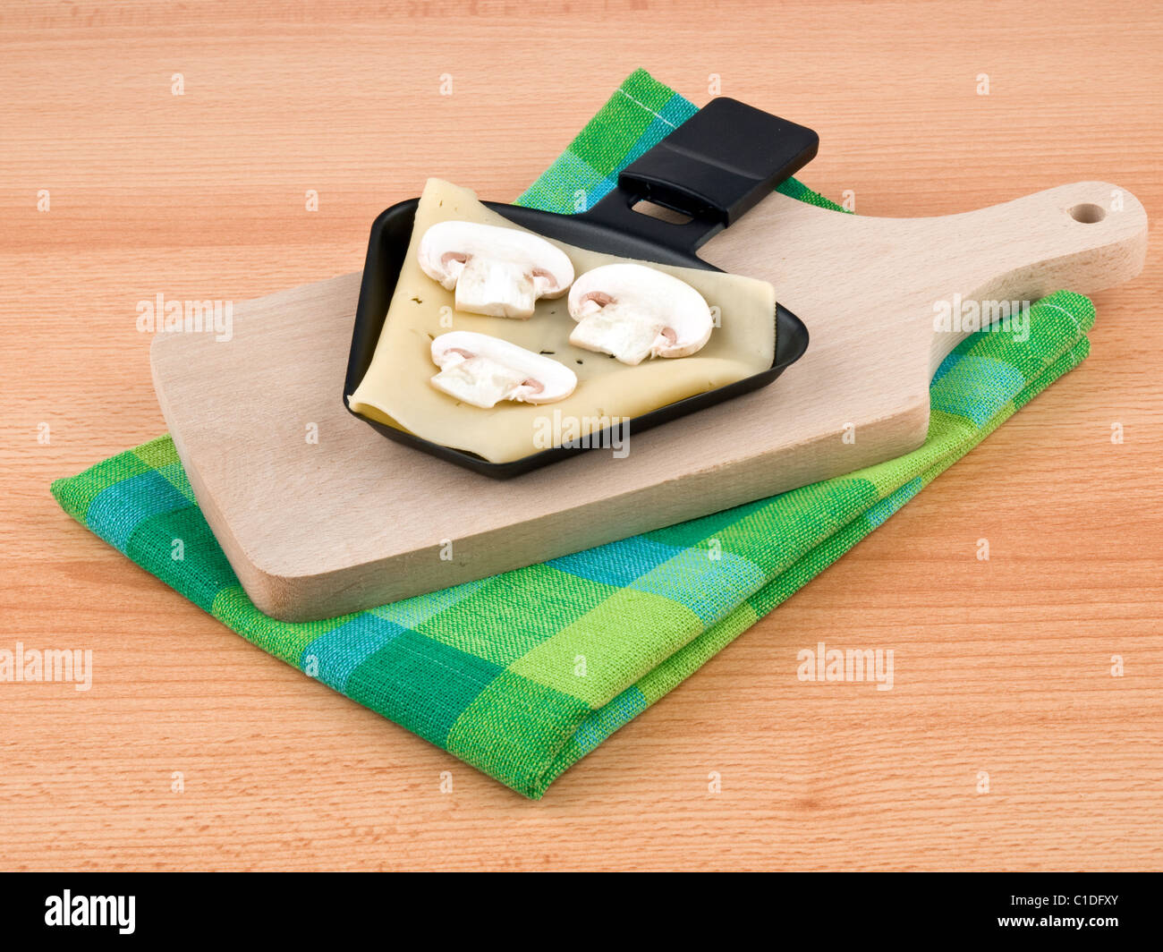 Raclette pan with edam cheese and sliced mushroom on chopping board ...