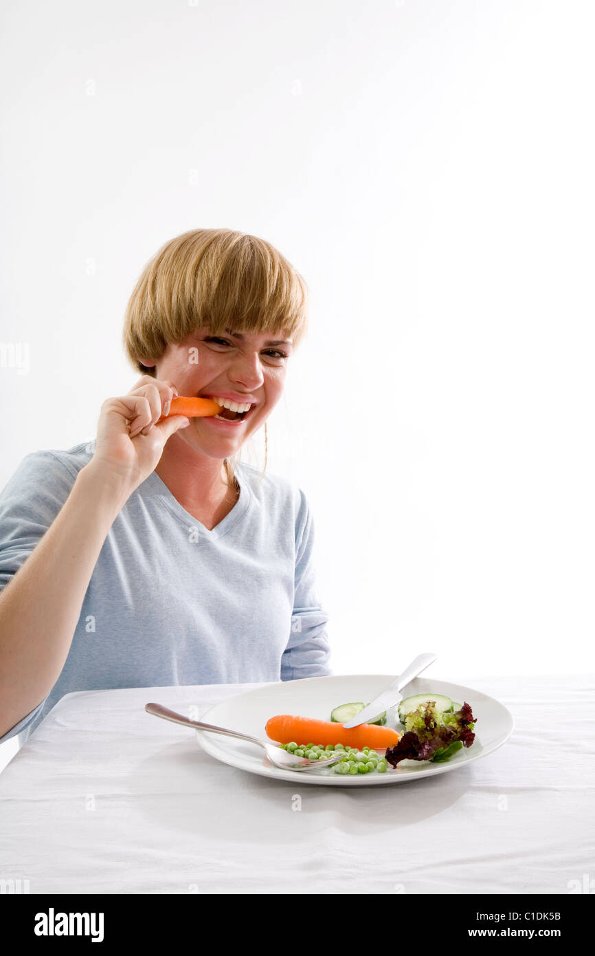 Young woman biting a carrot and eating plate of raw vegetables Stock ...