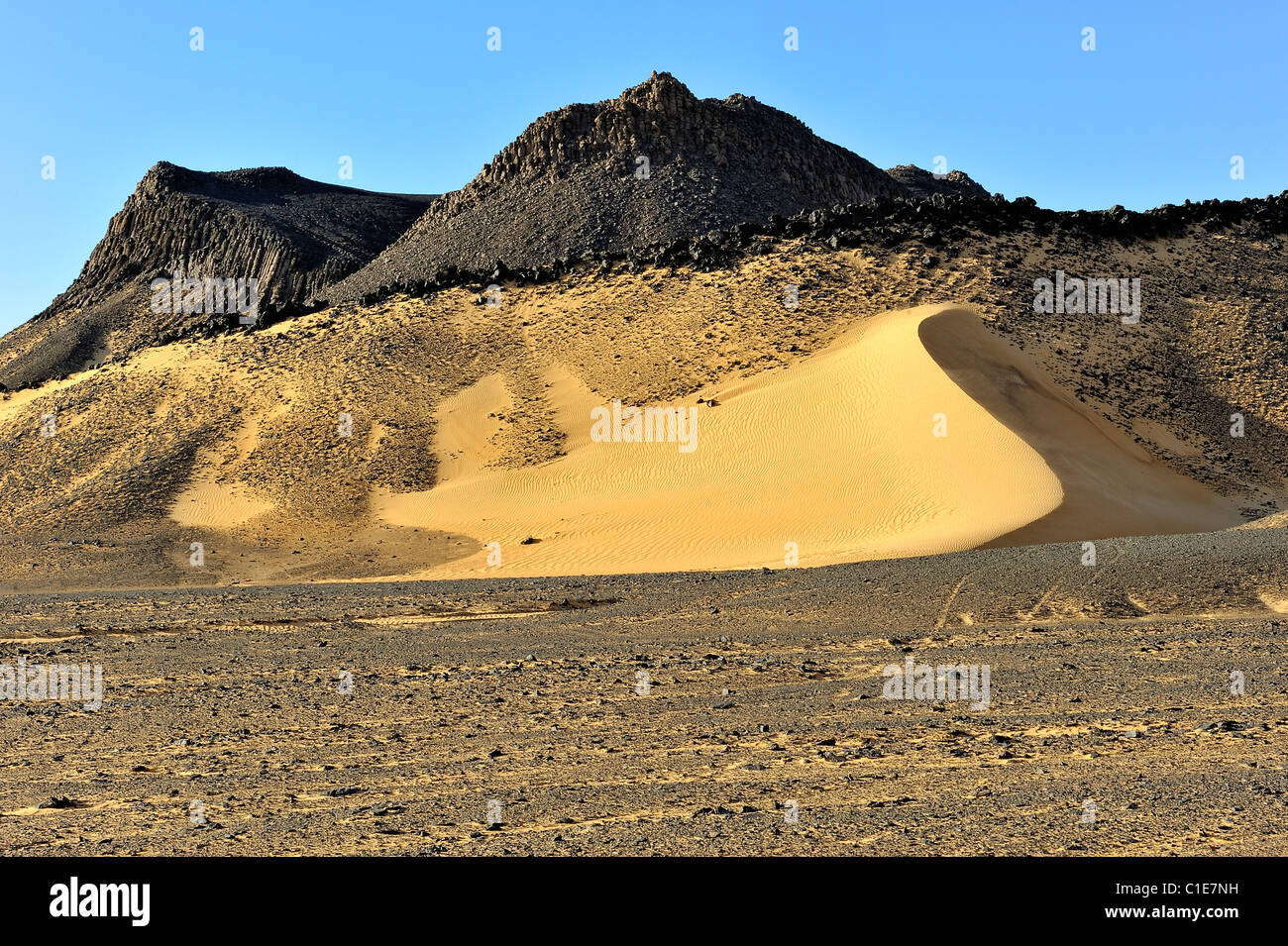 Mountain of volcanic origin and sand dunes in the Black Desert, Lybian ...