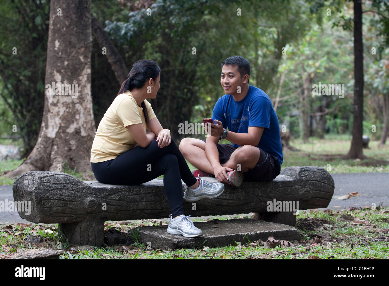 couple seated on a concrete park bench sharing smart phone Stock Photo - Alamy