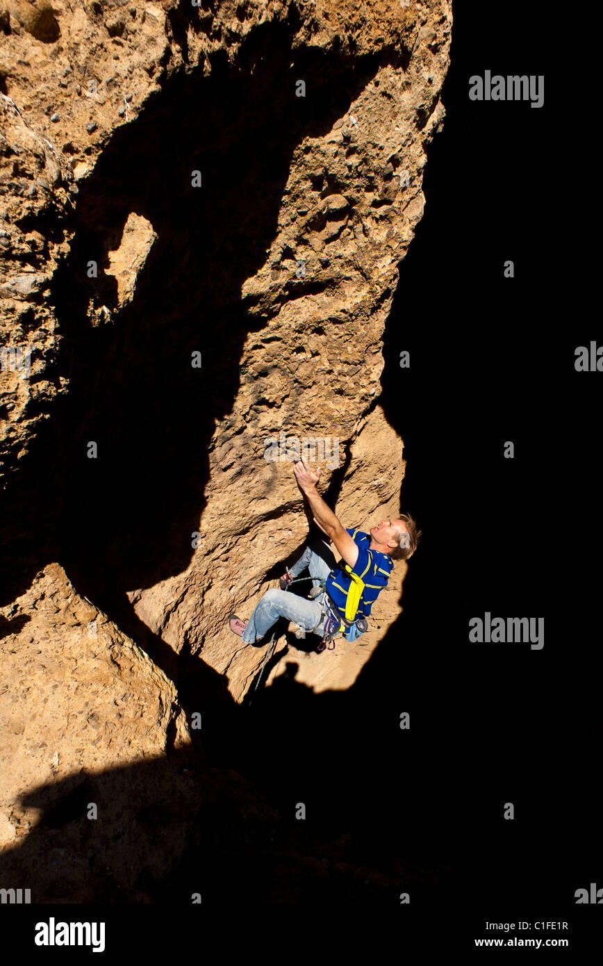 Male rock climber clings to the edge of a steep cliff as he struggles ...