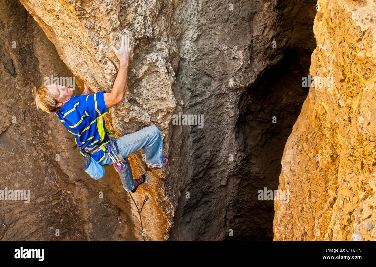 Male rock climber clings to the edge of a steep cliff as he struggles ...