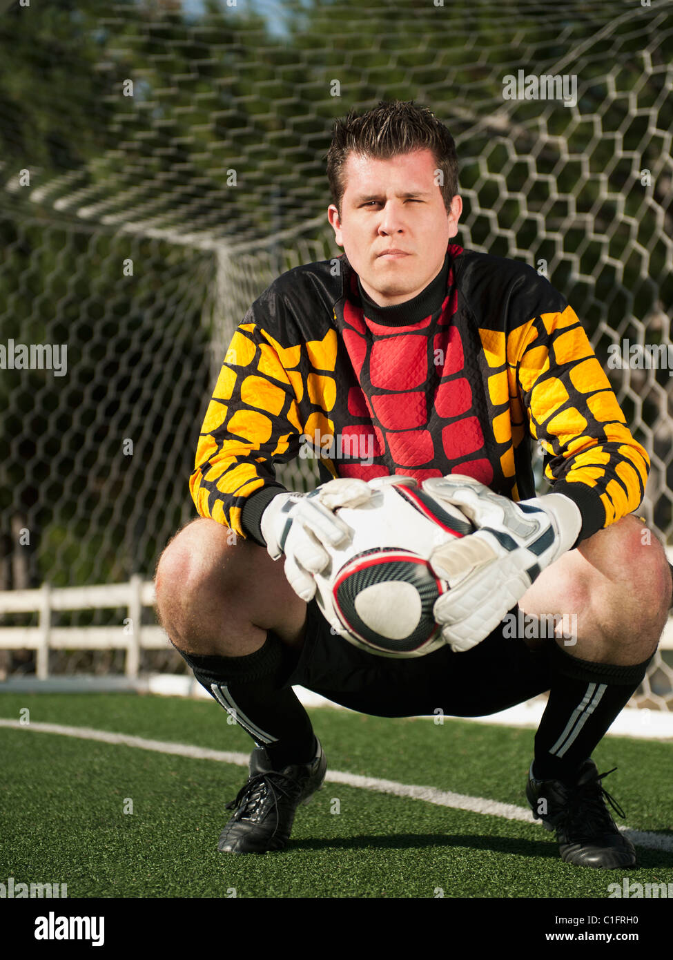 Mixed race goalkeeper crouching with soccer ball Stock Photo - Alamy