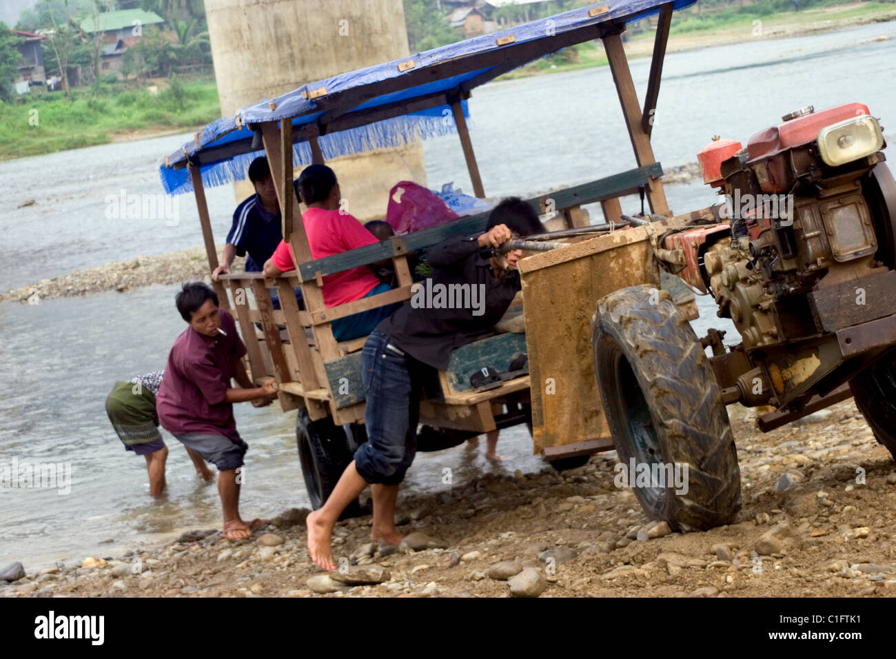 A group of Laotian people are pushing a tractor while crossing a river ...