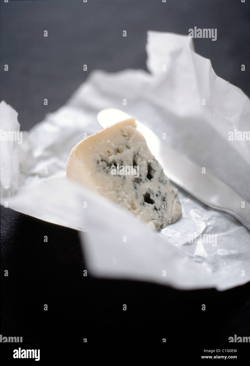 Close-up detail of unwrapped cheese in paper with a knife on a dark ...