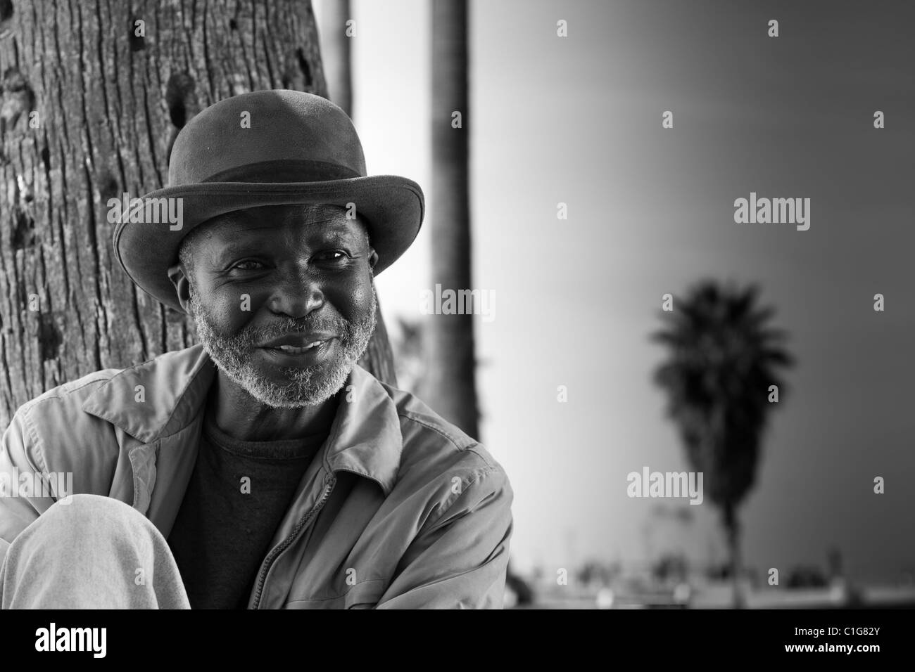 A photograph of a happy man relaxing against a tree at the beach Stock ...